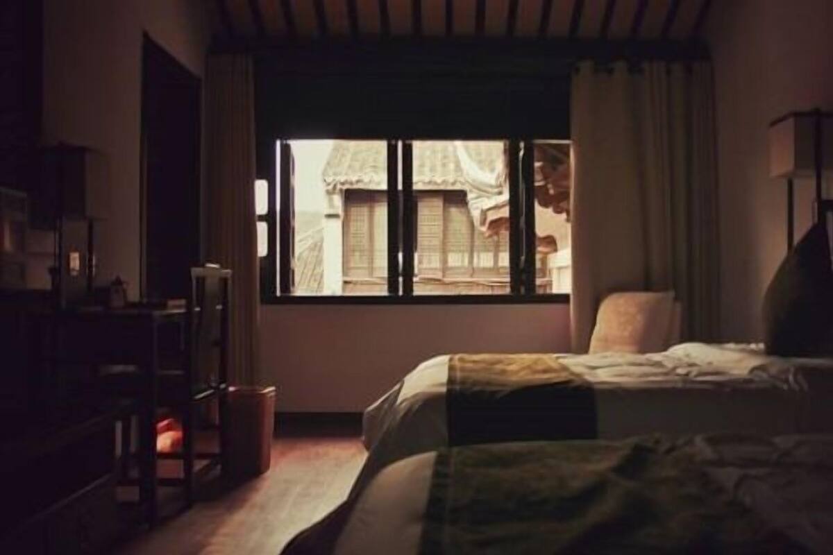 Um quarto com iluminação suave, uma cama, uma cadeira e uma janela com vista para um edifício.