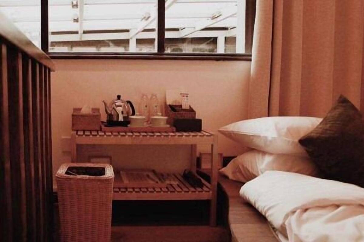 Quarto com cama, travesseiros, mesa de cabeceira e janela com cortinas.