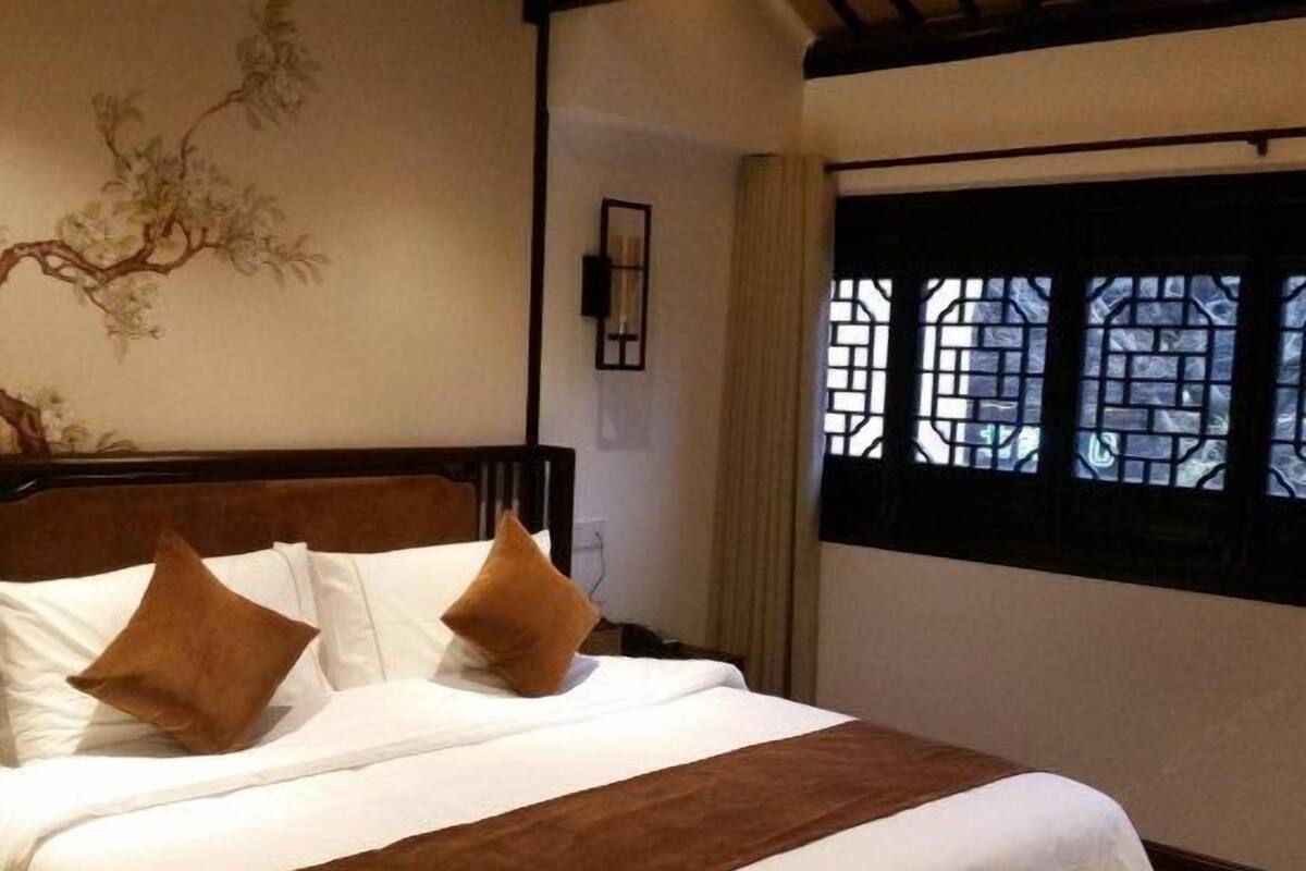 Quarto de hotel com uma cama, janela com padrão treliçado e parede com pintura de galho.