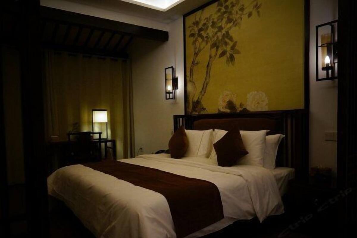 Quarto de hotel com uma cama grande, uma mesa com abajur e um quadro na parede.