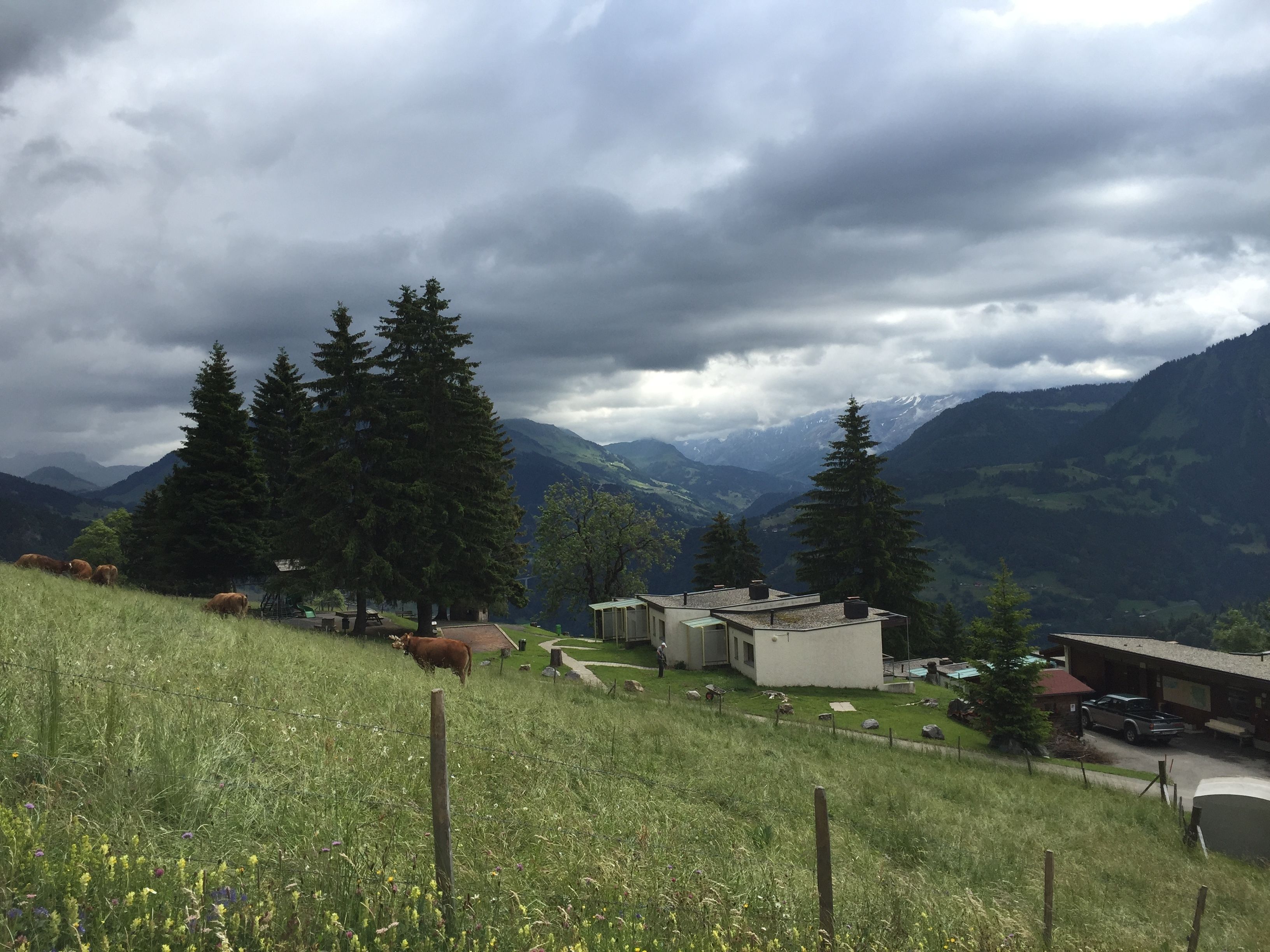Paisagem rural com uma casa, um campo cercado e montanhas ao fundo.
