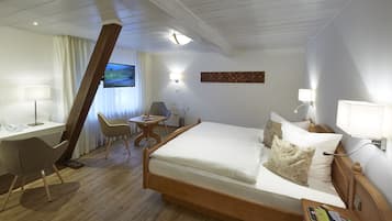 Quarto de hotel com uma cama grande, uma mesa com abajur, uma cadeira, uma TV e uma pequena mesa com um vaso.