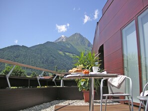 Varanda com mesa posta para o café da manhã, planta em vaso e vista para a montanha.