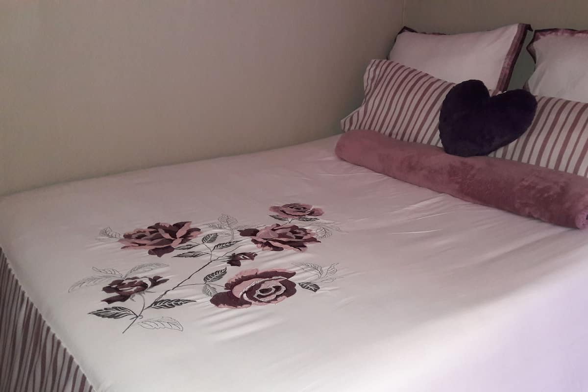 Cama bem arrumada com colcha florida, almofadas listradas e um travesseiro em formato de coração.