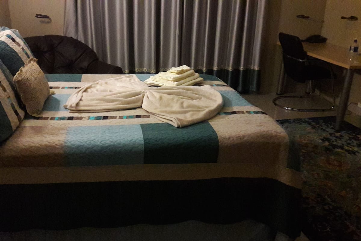 Quarto de hotel com cama, escrivaninha e cadeira.