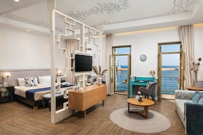Quarto de hotel moderno com cama, TV, escrivaninha, sofá e varanda com vista para o mar.
