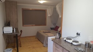 Quarto compacto com cozinha compacta, cama com dossel, mesa pequena e lixeira.
