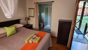 Quarto de hotel com cama, mesa de cabeceira, espelho, banheiro visível por uma porta aberta e varanda.
