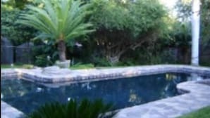 Uma piscina de borda curva, cercada por vegetação e uma moldura de pedra.