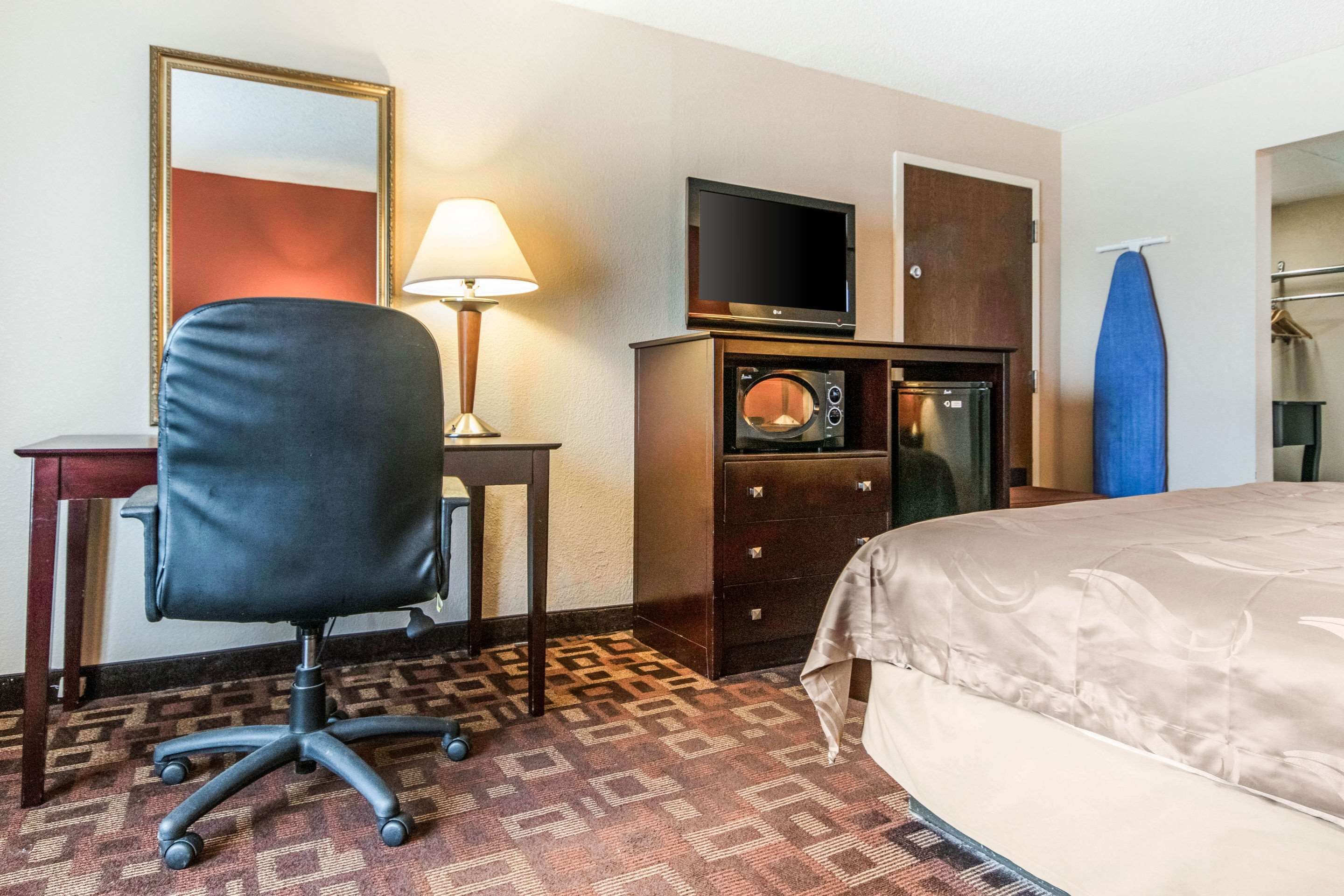 Quarto de hotel com cama, escrivaninha com cadeira, televisão, micro-ondas e cômoda.
