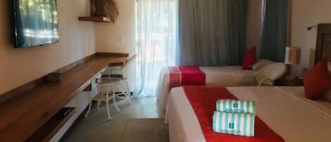 Quarto de hotel com cama, escrivaninha, cadeira, televisão e janela com cortinas.