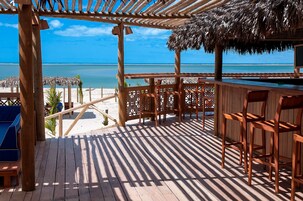 Um deck de madeira com telhado de palha, com vista para uma praia e oceano.