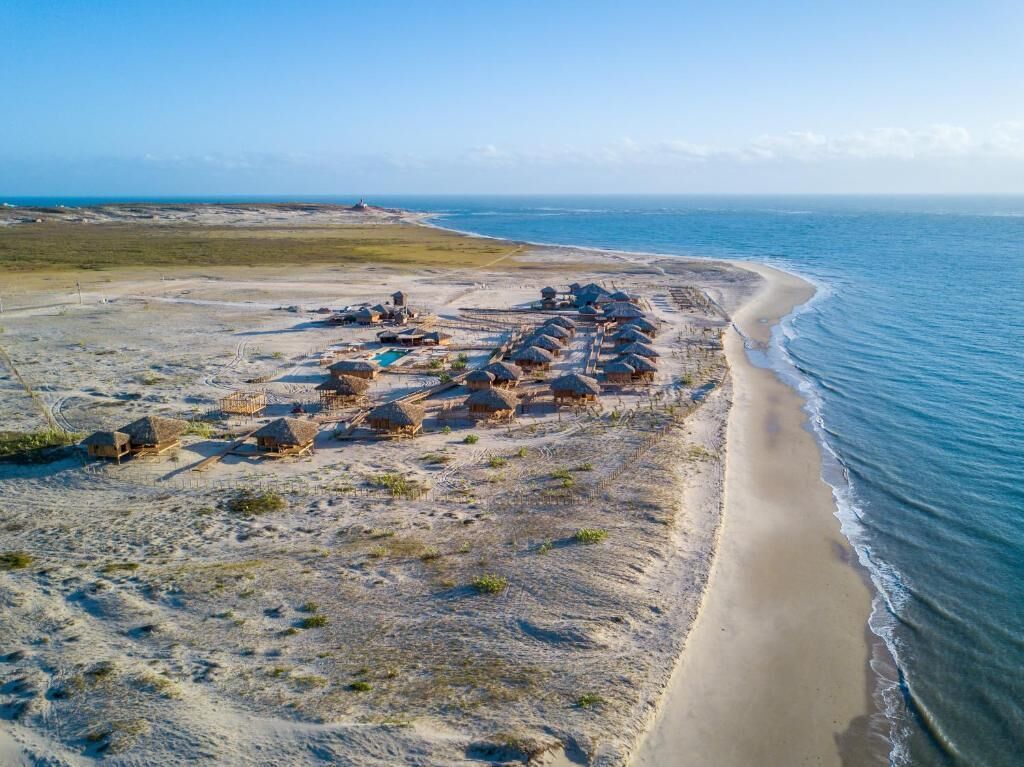 Um resort à beira-mar com cabanas de telhado de palha dispostas em semicírculo, com vista para o oceano.