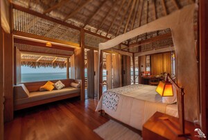 Quarto com cama, um assento à janela com almofadas, luminária e vista para o mar.