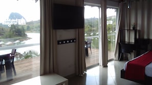 Quarto de hotel com uma janela grande, uma cama, uma televisão e uma mesinha.