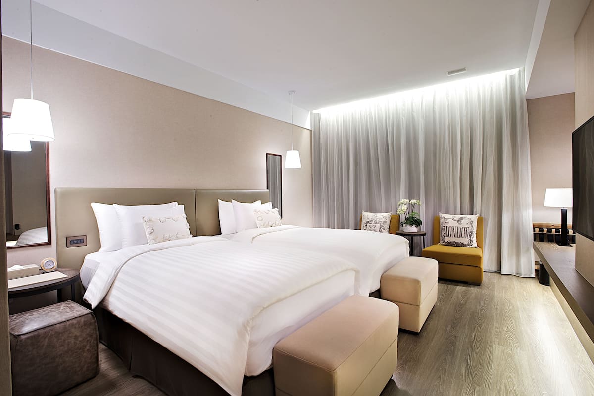 Quarto de hotel com cama grande, mesa de cabeceira, cadeira, escrivaninha e espelho.