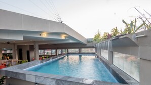 Piscina interior moderna com deck de concreto, rodeada por área coberta com assentos e vista para a cidade.