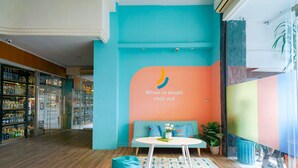 Interior vibrante com parede azul-turquesa e laranja, uma mesa branca com almofada azul, e um balcão de vidro à esquerda.
