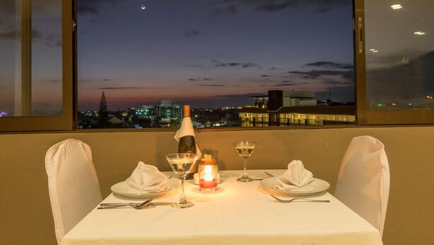 Mesa posta para dois, com garrafa de vinho, duas taças, uma vela e vista da cidade ao entardecer.