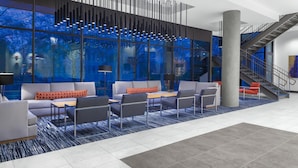 Um lobby moderno com área de sofás, escada e grandes janelas.
