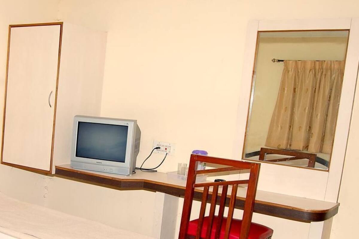 Um quarto pequeno com uma escrivaninha, uma cadeira, uma televisão e um espelho.