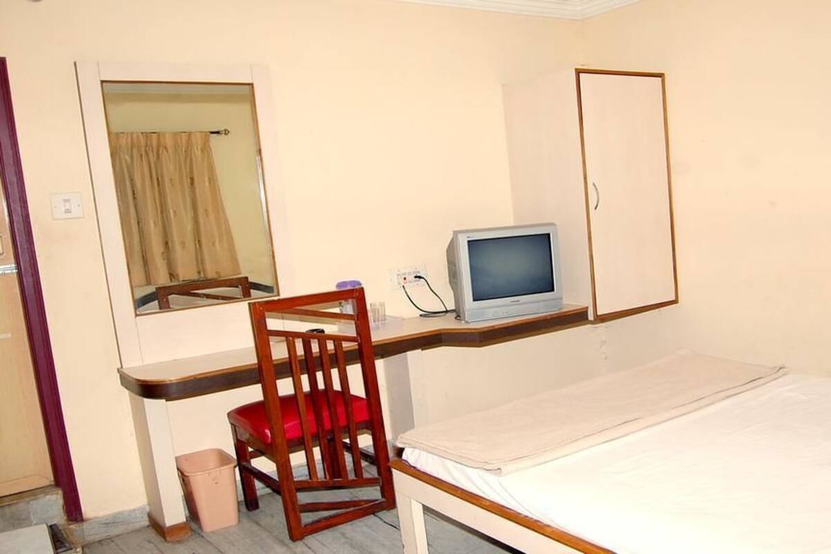 Quarto com cama, escrivaninha com computador, cadeira, guarda-roupa e espelho.