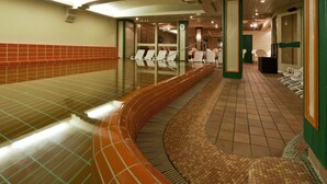 Um saguão de hotel com uma área de estar em curva, piso ladrilhado e porta com moldura verde.
