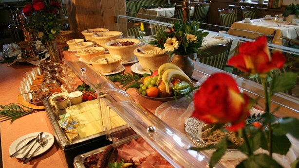 Buffet com diversos alimentos, incluindo carnes, queijos, frutas e flores.