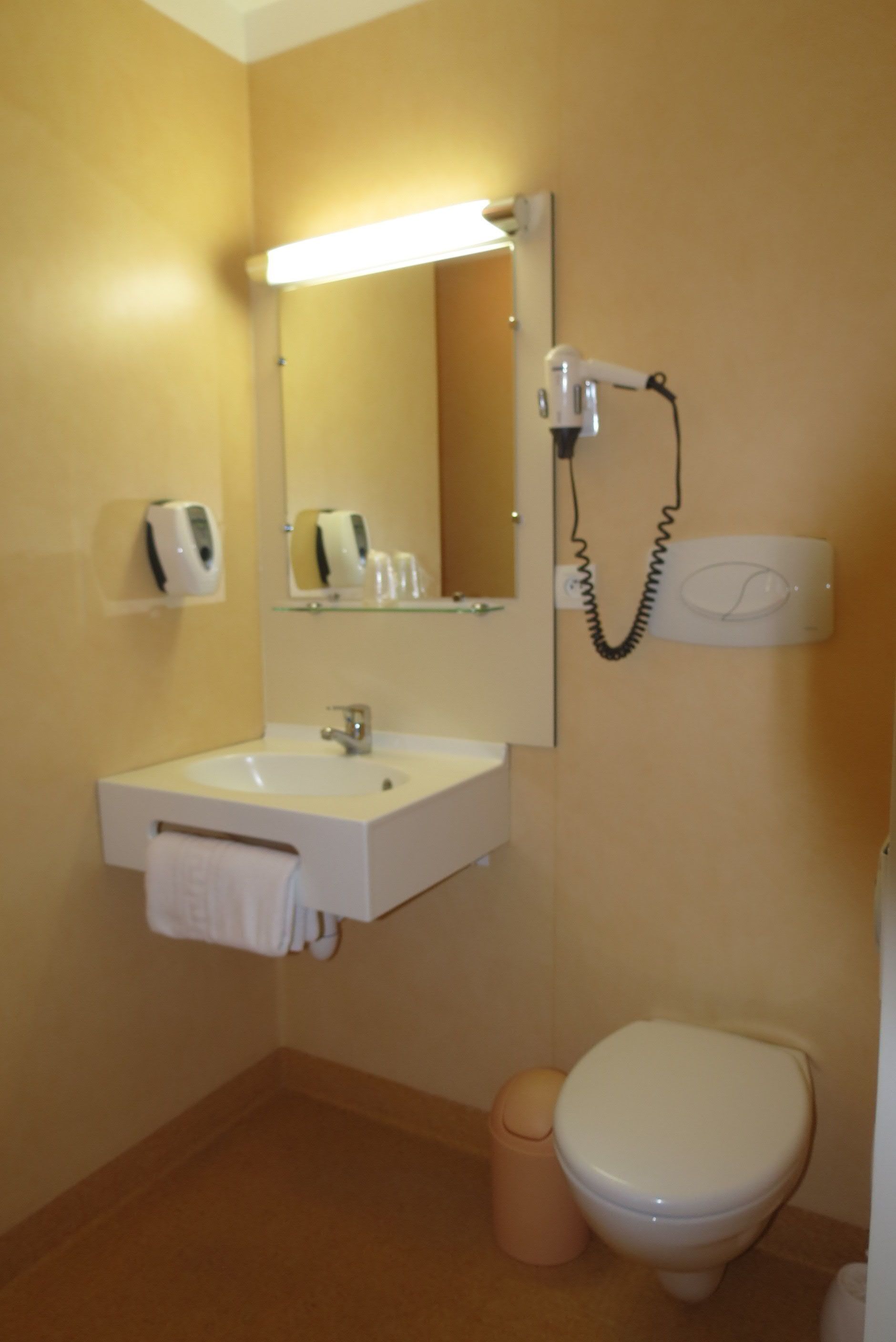 Casa de banho com lavatório, espelho, secador de cabelo e sanita.