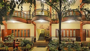Um átrio de vários níveis com uma escadaria central, rodeado por plantas em vasos e um guarda-corpo decorativo.