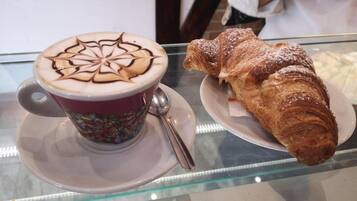 Uma chávena de café com arte de latte num pires e um croissant num prato.