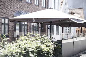 Um guarda-chuva de hotel com a inscrição 'HOTEL RESTAURANT', em frente a uma fachada de tijolos com grandes janelas.