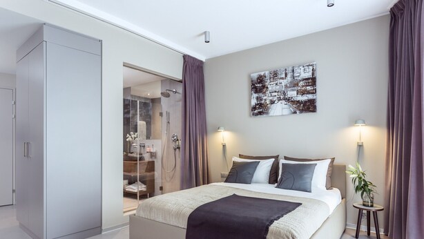 Quarto moderno com uma cama grande, um closet espaçoso e um banheiro visível através de uma porta de vidro.