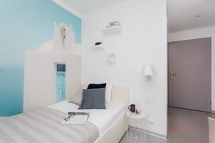 Quarto moderno com uma cama, uma mesinha de cabeceira, um criado-mudo e uma prateleira fixada na parede, além de uma porta.