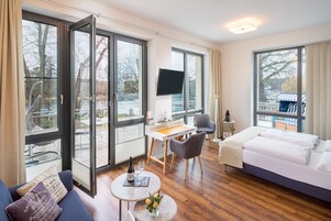Quarto de hotel moderno com uma cama grande, uma escrivaninha, um sofá e uma televisão.