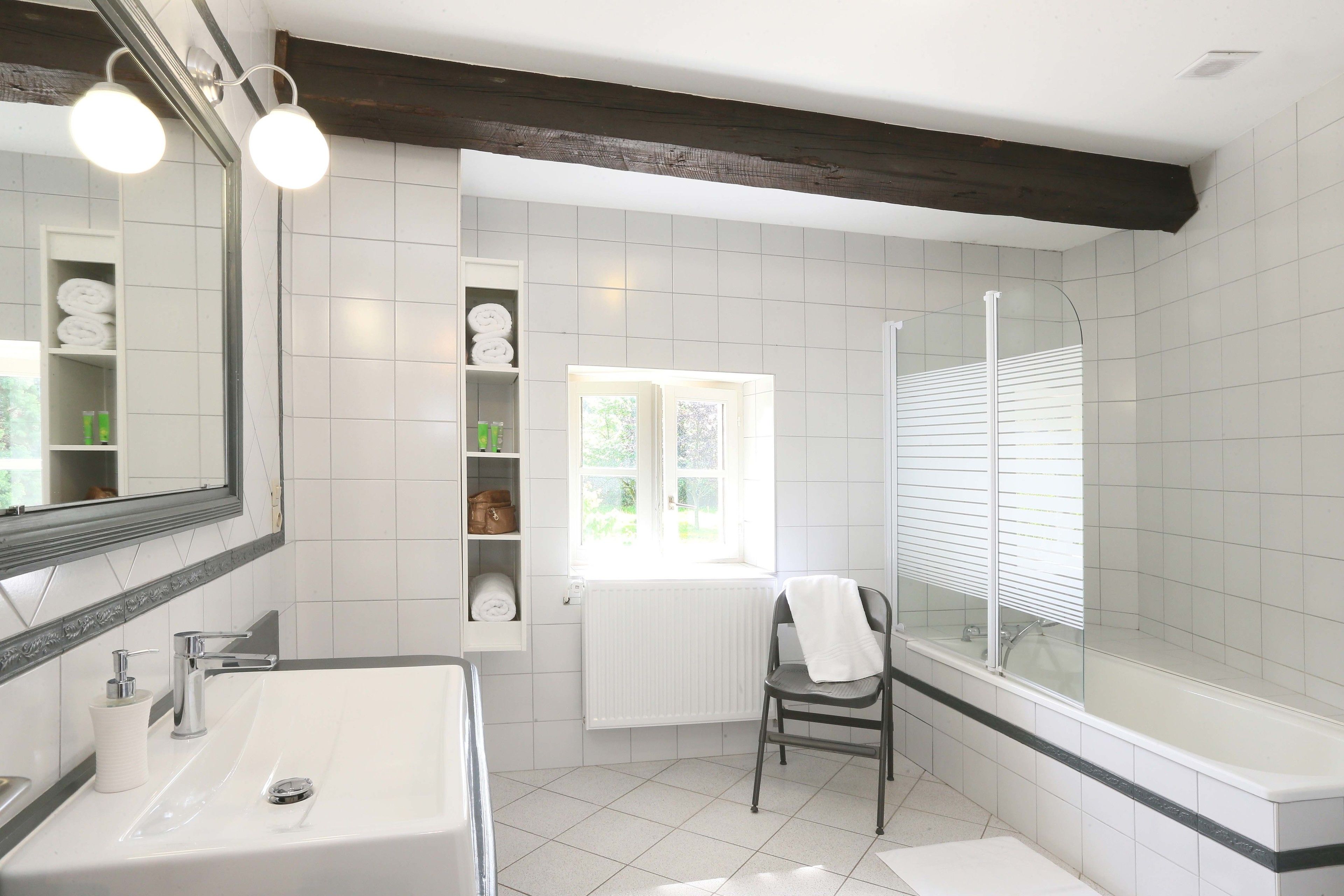 Casa de banho moderna com lavatório branco, espelho, chuveiro e janela com persianas.