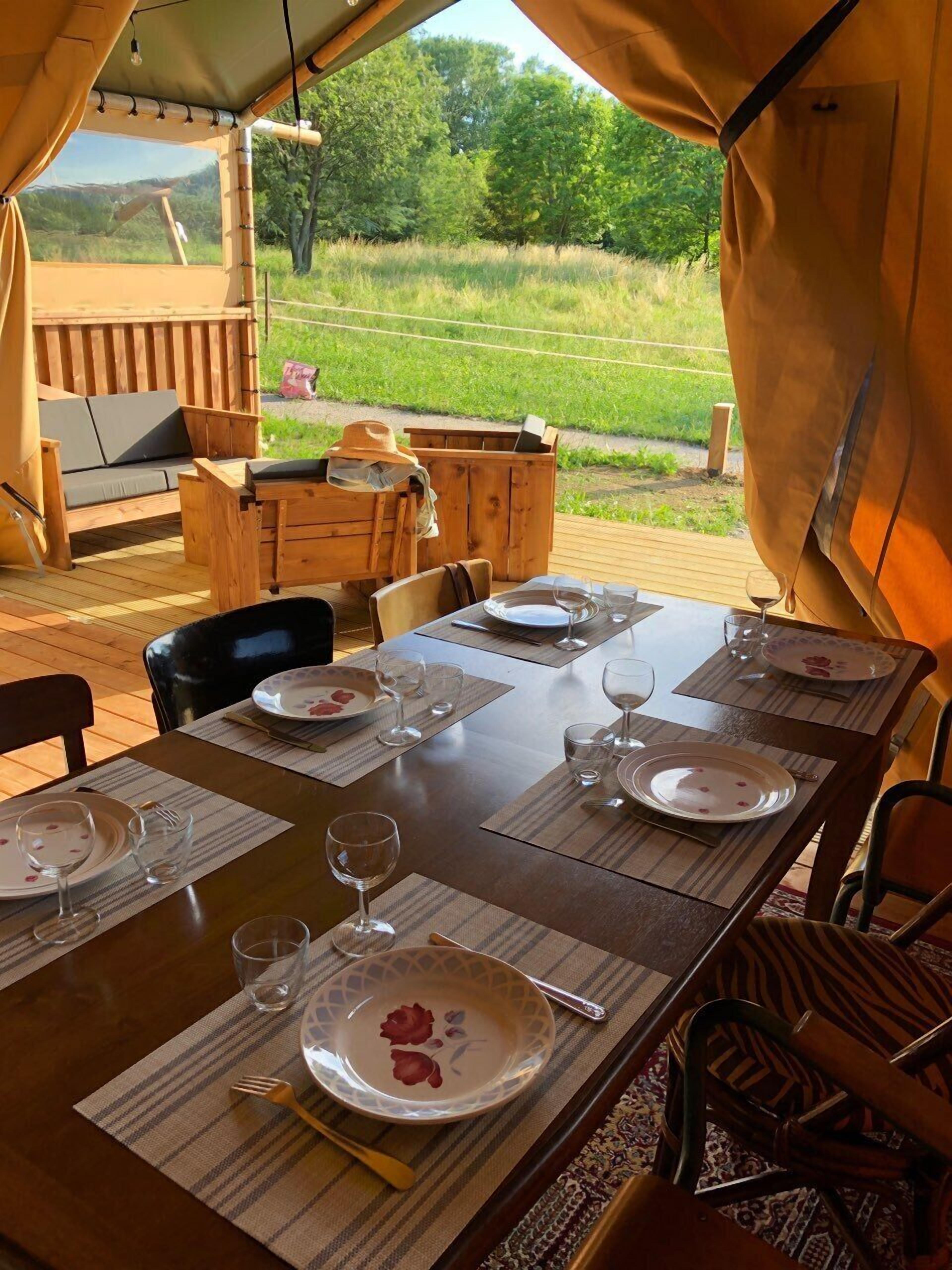 Uma área de refeições com mesas preparadas para quatro pessoas, assentos ao ar livre e vista para um campo gramado.