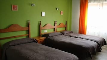 Quarto com três camas de madeira encostadas a uma parede verde, cada uma com cabeceira de madeira e uma pequena mesa de cabeceira.