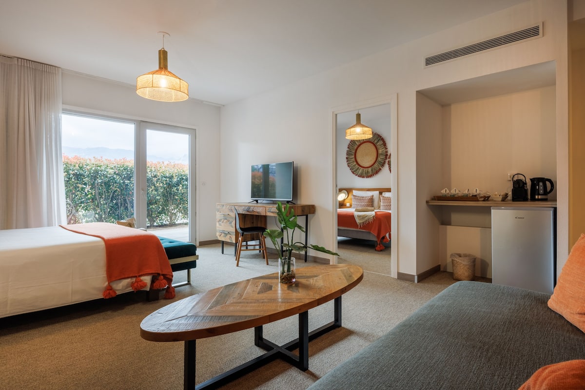Quarto de hotel moderno com cama, sofá, mesa de jantar, escrivaninha e cozinha compacta.
