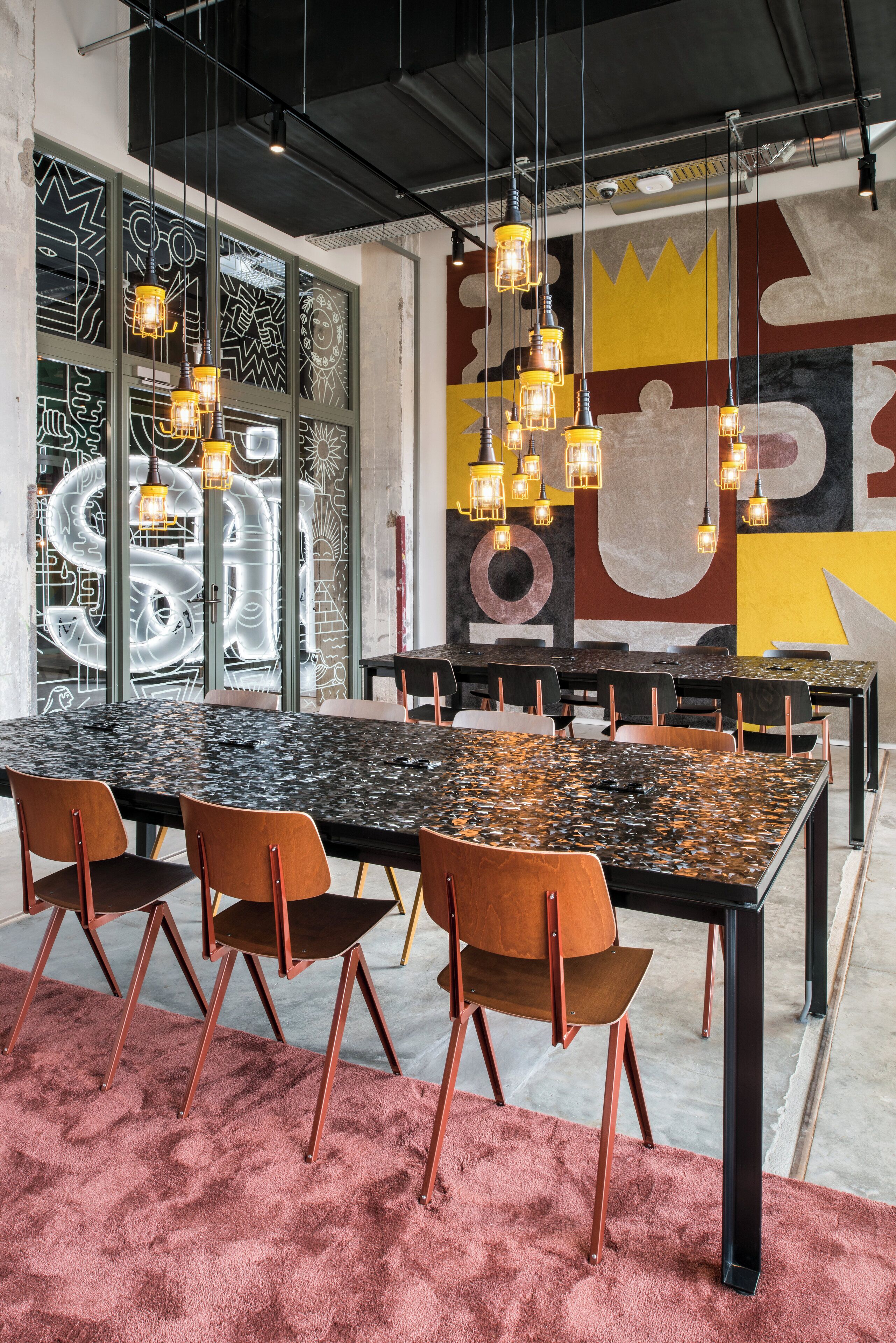 Uma área de jantar moderna com mesa de mármore preto, cadeiras de madeira e iluminação pendente.