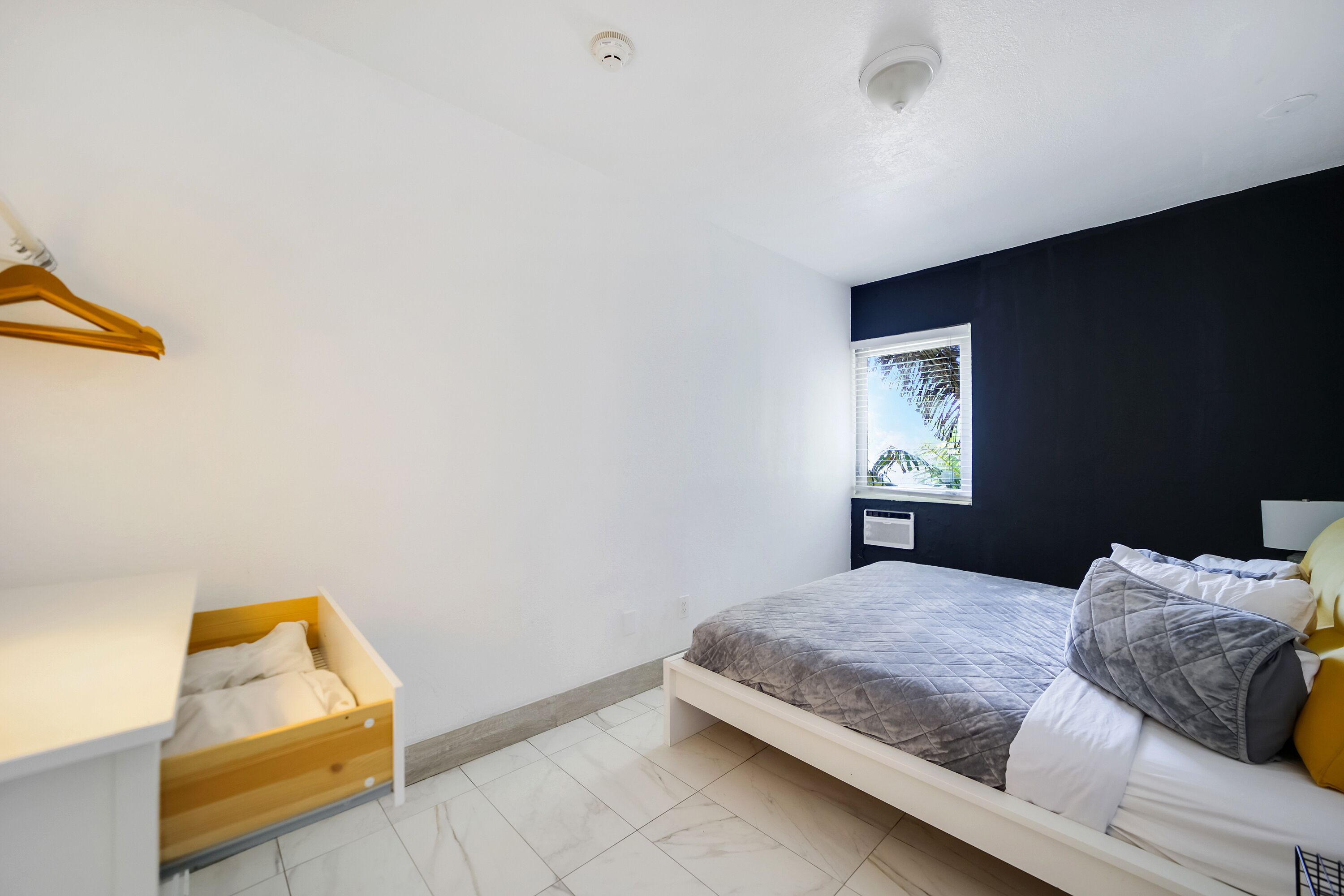 Quarto com cama, cômoda de madeira, janela com vista e luminária no teto.