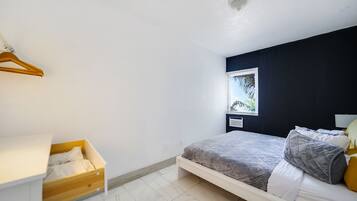 Quarto com cama, cômoda de madeira, janela com vista e luminária no teto.