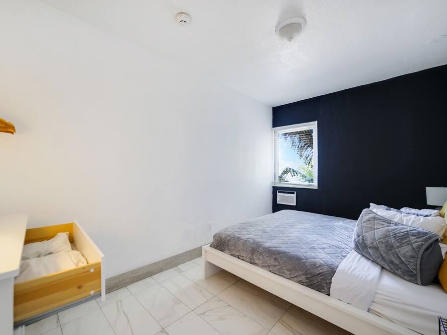 Quarto com cama, cômoda de madeira, janela com vista e luminária no teto.