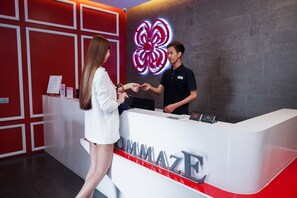 Uma receção com esquema de cores vermelho e branco, uma decoração de flor em néon na parede, e um sinal que diz "OMMAZE".