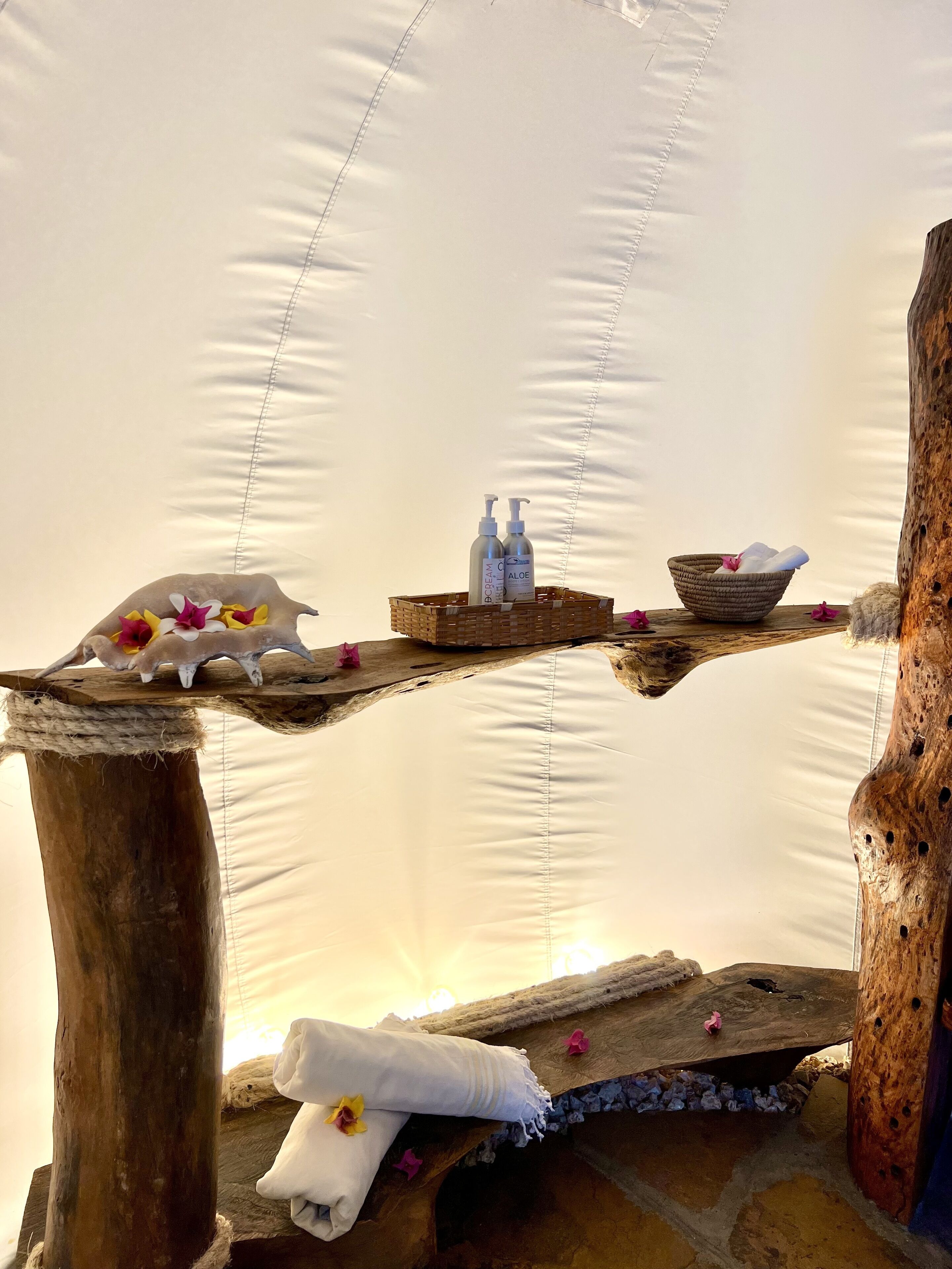 Uma árvore para gatos de madeira com uma toalha e um pequeno cesto no topo, e uma parede branca ao fundo.
