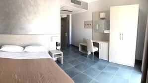 Quarto de hotel com cama, mesa de cabeceira, cadeira, guarda-roupa e pequena escrivaninha.