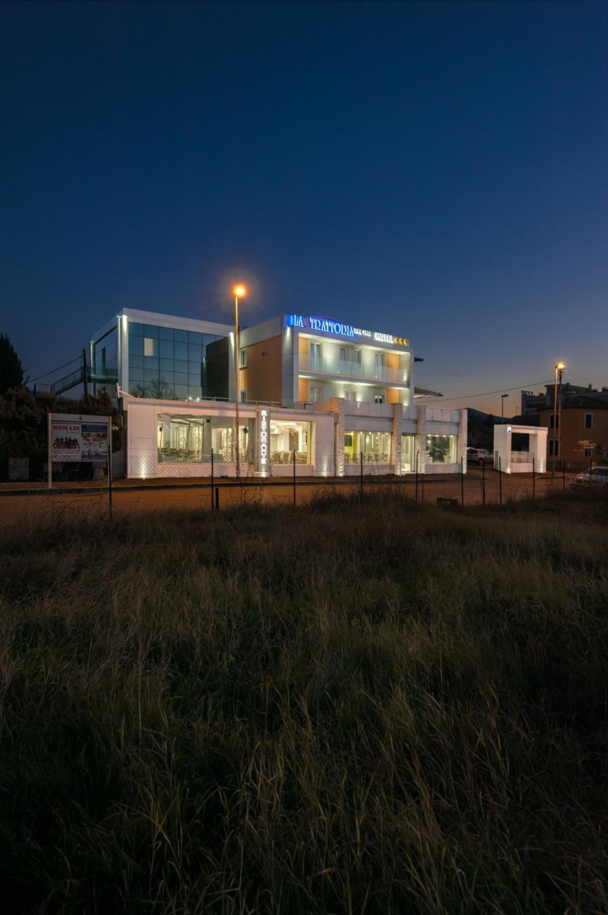 Um hotel moderno com fachada de vidro, vários andares e uma entrada bem iluminada.