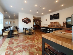 Um café com piso de mármore, várias áreas de estar, uma máquina de café e uma televisão de tela plana na parede.