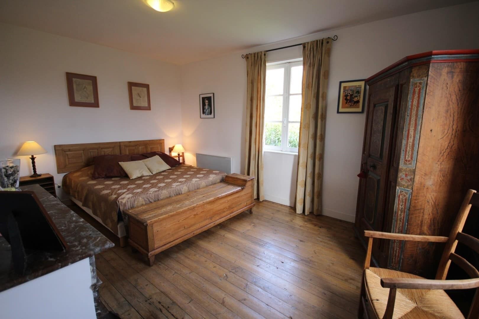 Quarto com cama de madeira, mesa de cabeceira com abajur, guarda-roupa de madeira e uma cadeira.