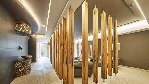 Um interior moderno com um corredor comprido, divisórias de madeira, piso ladrilhado e uma área de estar com sofá.